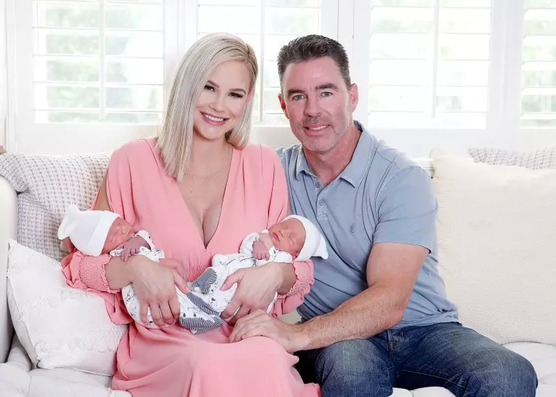 auténticas amas de casa do alumbre do condado de Orange, meghan king edmonds, sostén aos seus xemelgos recén nacidos con un vestido fluído de manga longa con escote en V rosa salmón mentres que o seu marido, jim edmonds, leva un polo azul e vaqueiros.