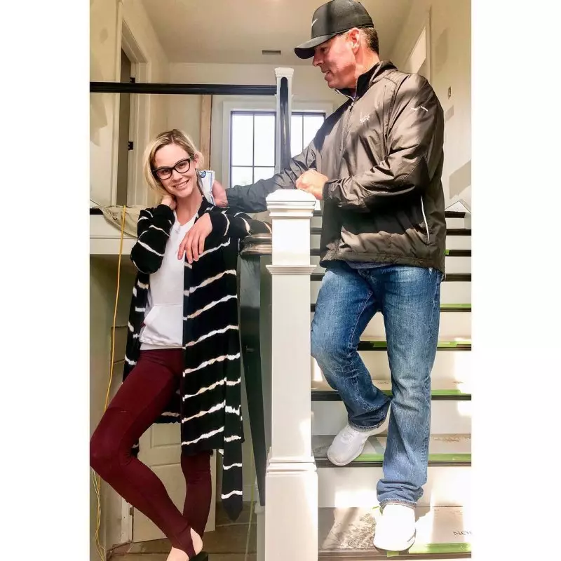 meghan king edmonds ngagem legging anggur sanggurdi sareng kaos bodas sareng baju haneut hideung bodas bari jim edmonds nganggo topi nike hideung, jaket windbreaker coklat, jeans sareng sneakers bodas