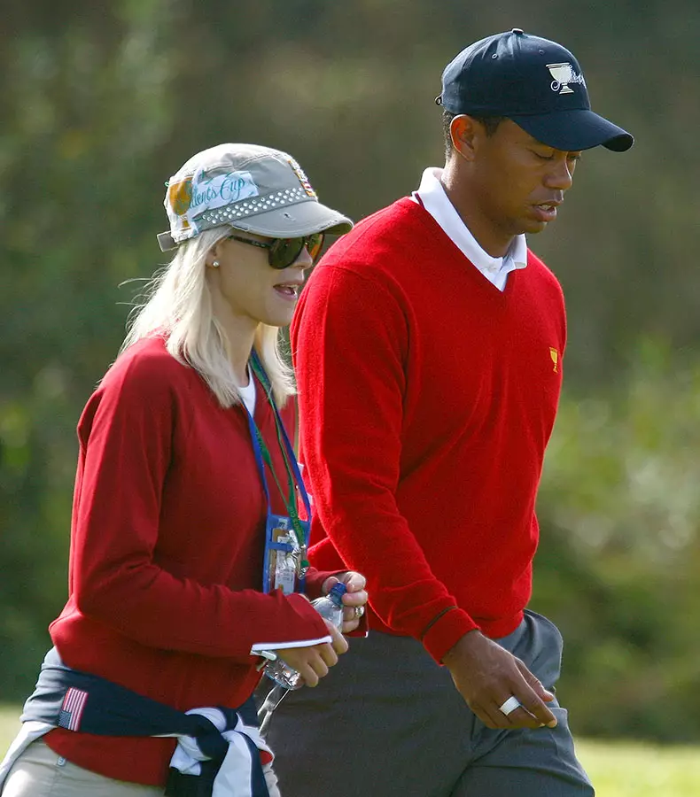 Tiger Woods e Elin Nordegren camiñan durante o primeiro día dos partidos en cuarteto da Copa Presidents usando camisas vermellas e gorras de béisbol a xogo