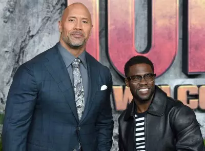 Kevin Hart trägt eine Brille mit einer Lederjacke, während er mit Dwayne Johnson in einem Anzug auf dem roten Teppich posiert